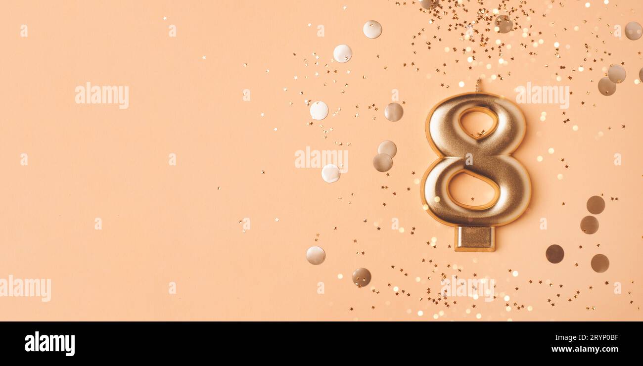 Gold candle in the form of number eight on peach background with ...