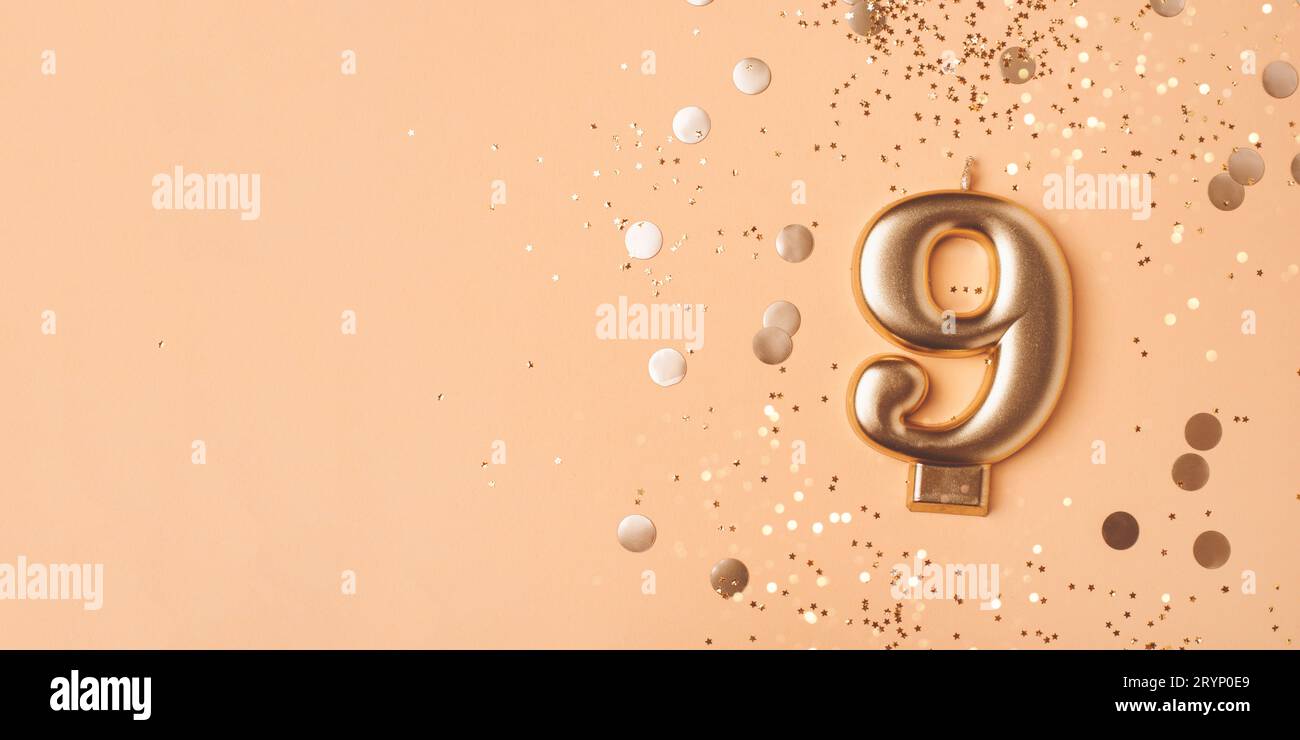 Gold candle in the form of number nine on peach background with ...
