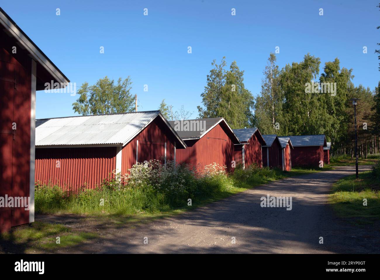 Red wooden buildings, and boathouses along a gravel road. Summer ...