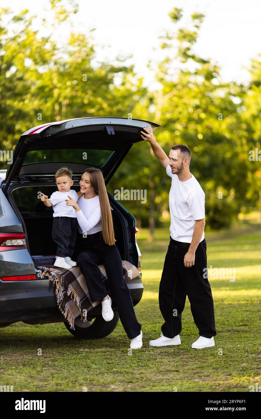 Side view of the family sitting in the car trunk outside the city ...
