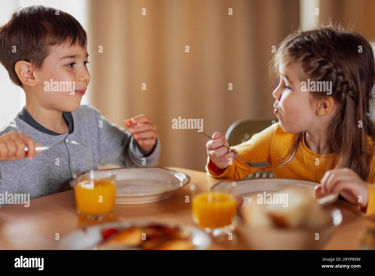 Two small children are sitting at dining table and having breakfas ...