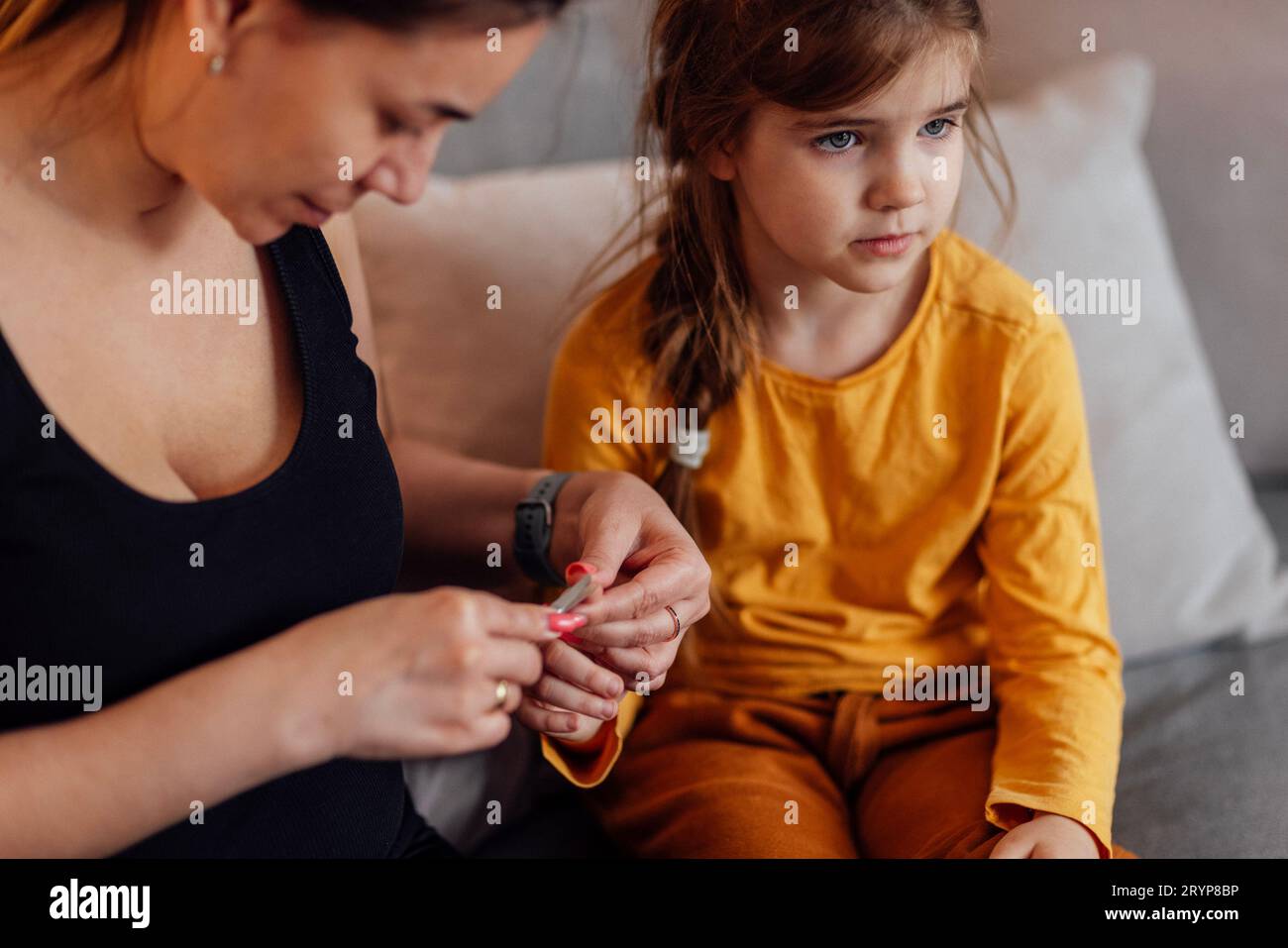 Young mother trims the nails on the hands of her cute daughter with ...