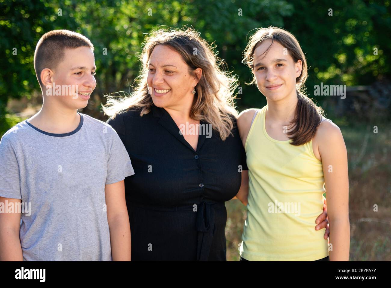 Portrait of happy mother and her teen twins standing and smiling in the ...