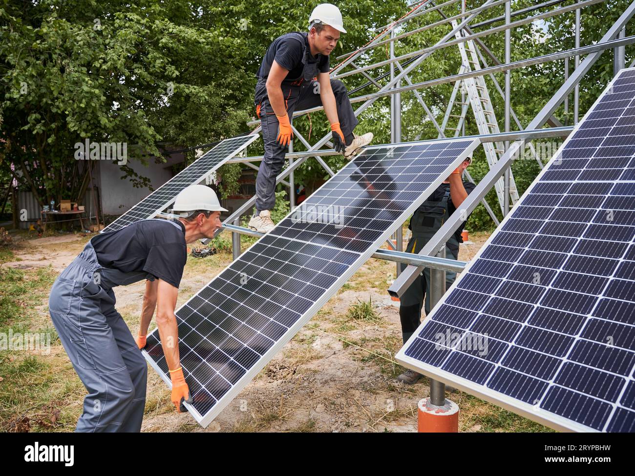 Three men solar installers wearing safety helmets and work overalls ...