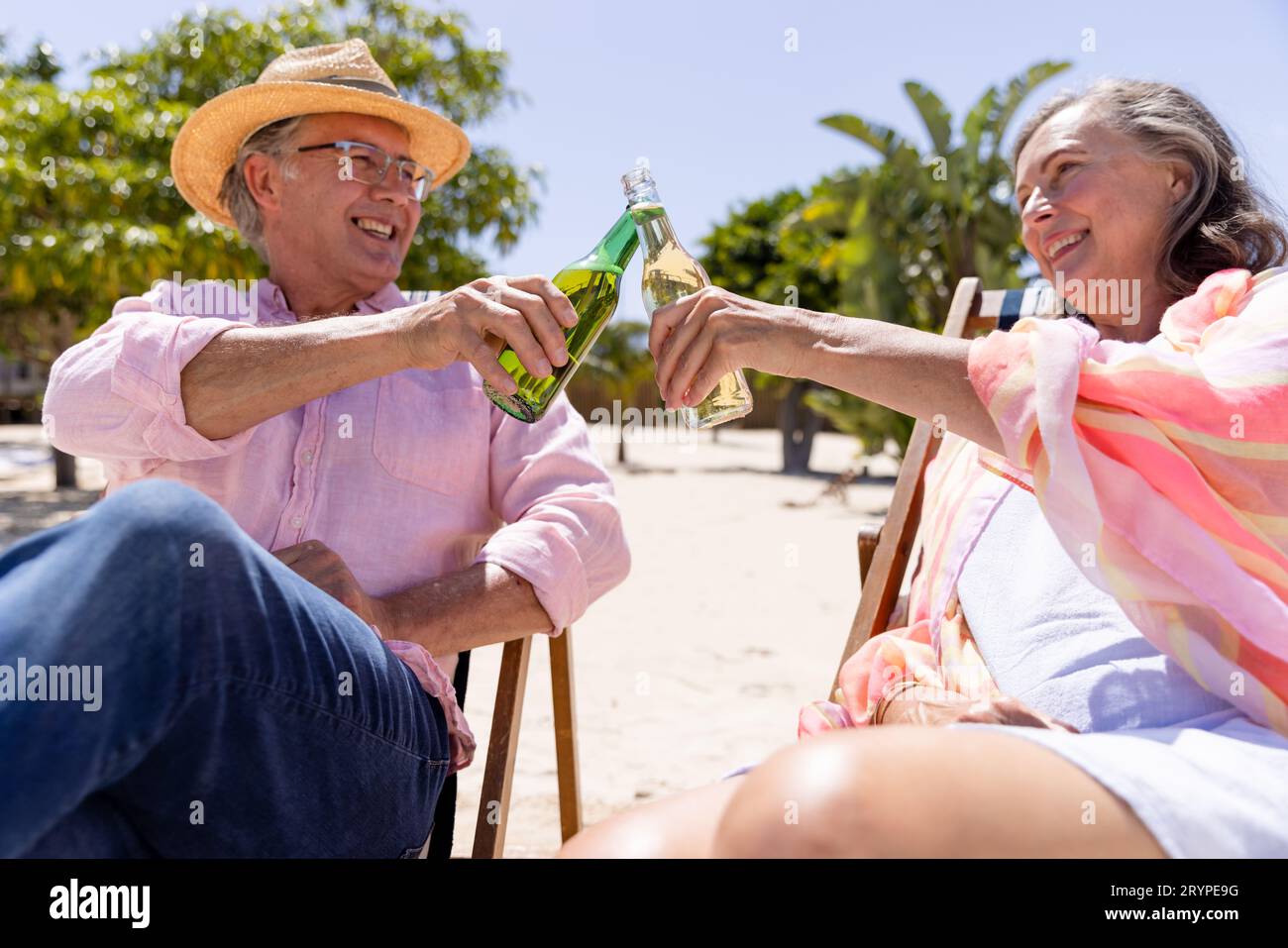 Smiling caucasian senior couple toasting beer bottles while sitting on ...