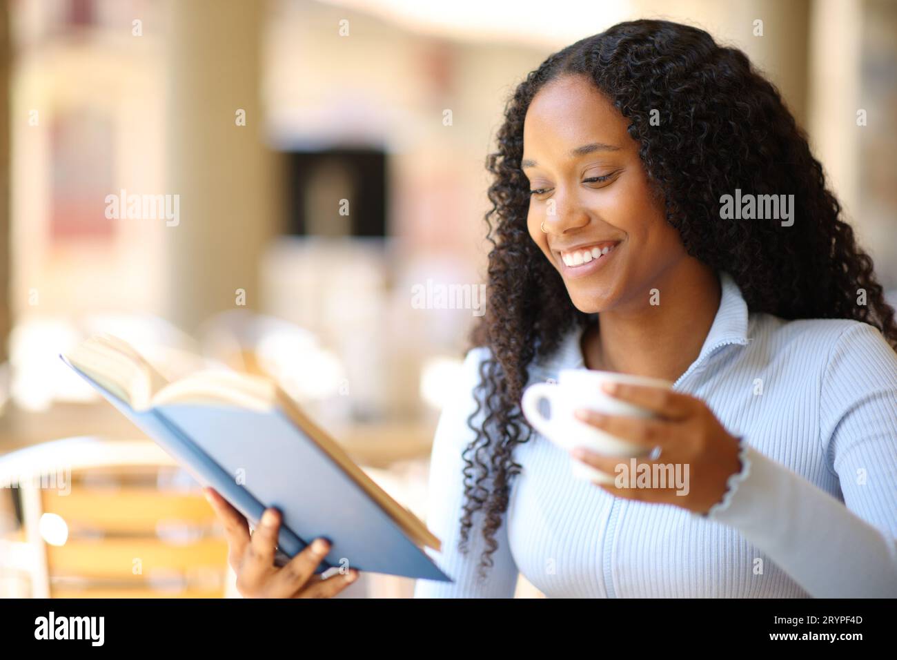 Happy black woman reading a paper book sitting in a coffee shop terrace ...