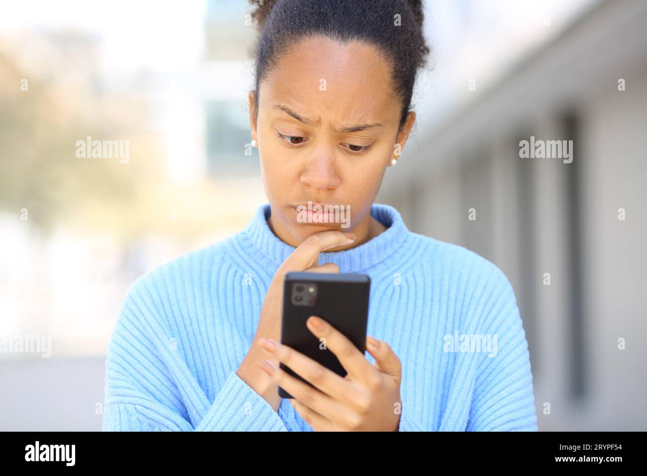 Front view portrait of a worried black woman checking phone in the street Stock Photo - Alamy