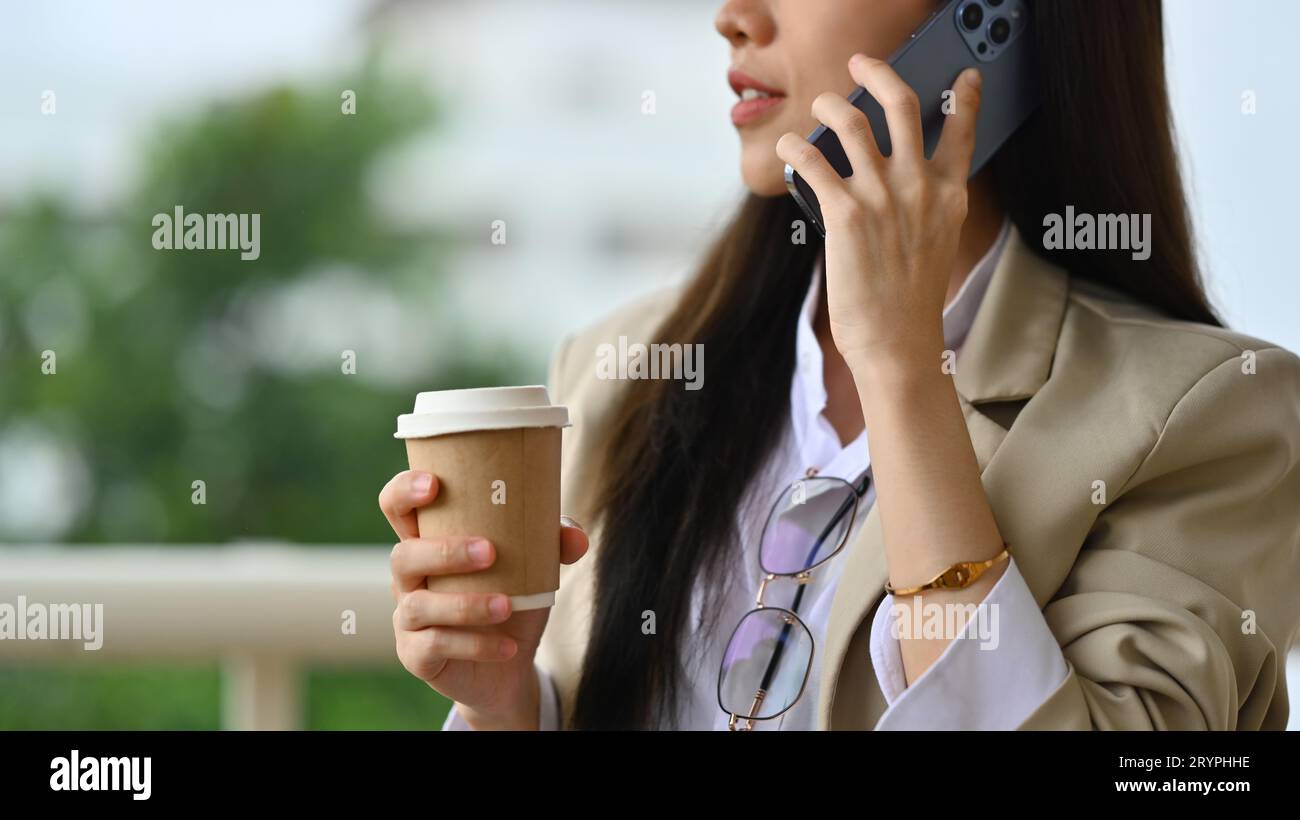 Modern businesswoman with disposable paper coffee cup talking on mobile ...