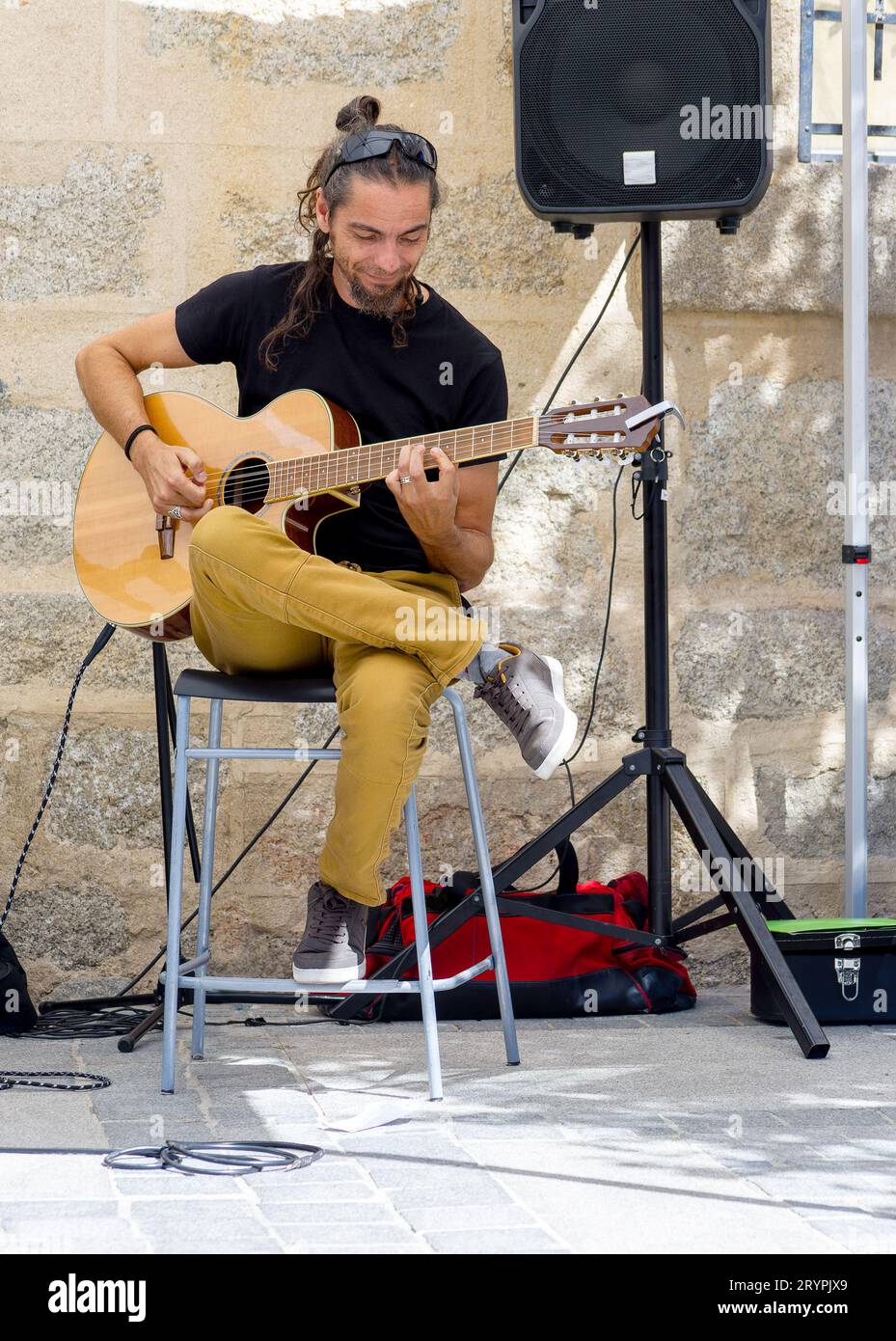 man sitting on a stool in an outdoor setting, playing an acoustic ...