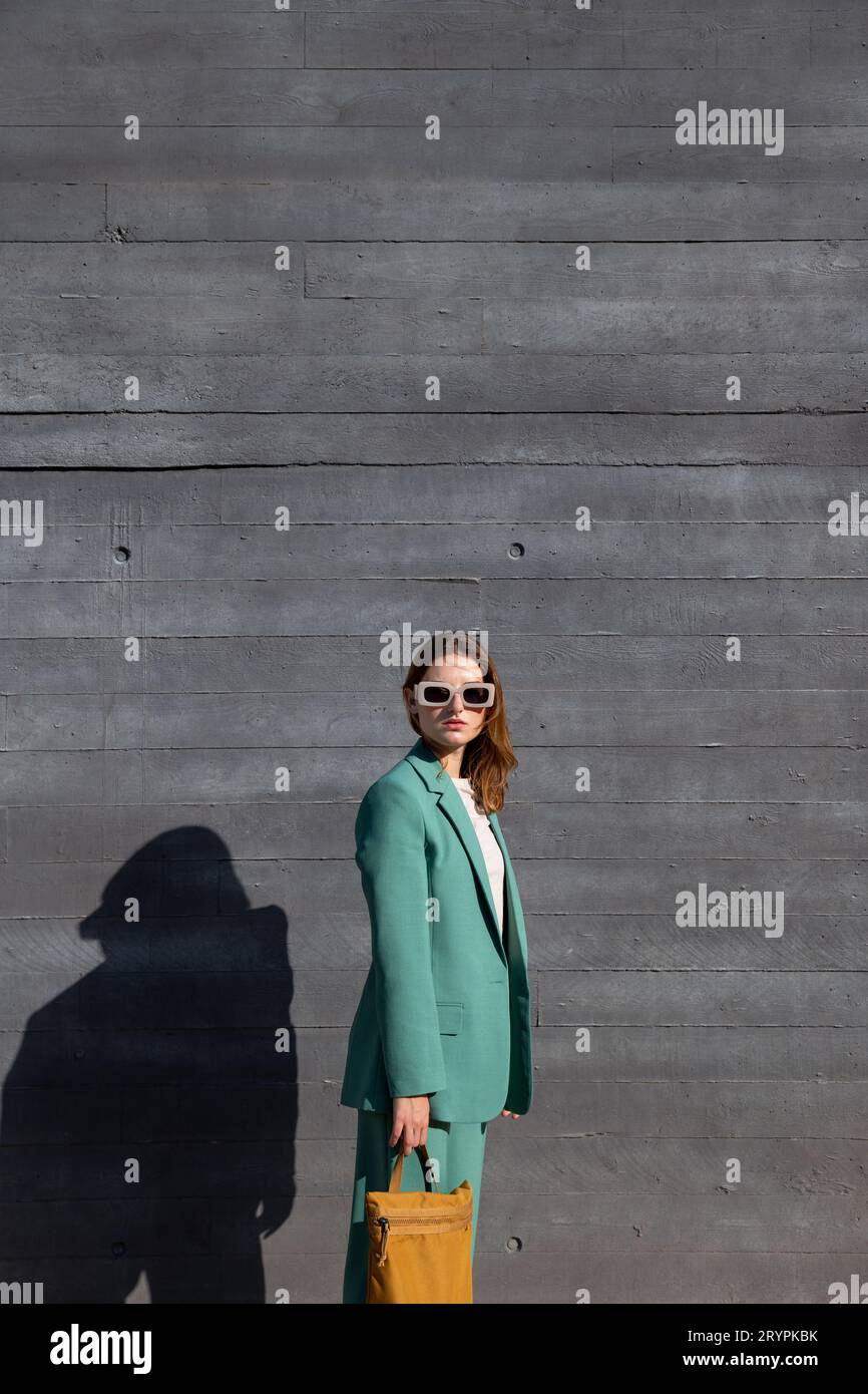 Young empowered ginger-haired woman in green suit, white sunglasses and ...
