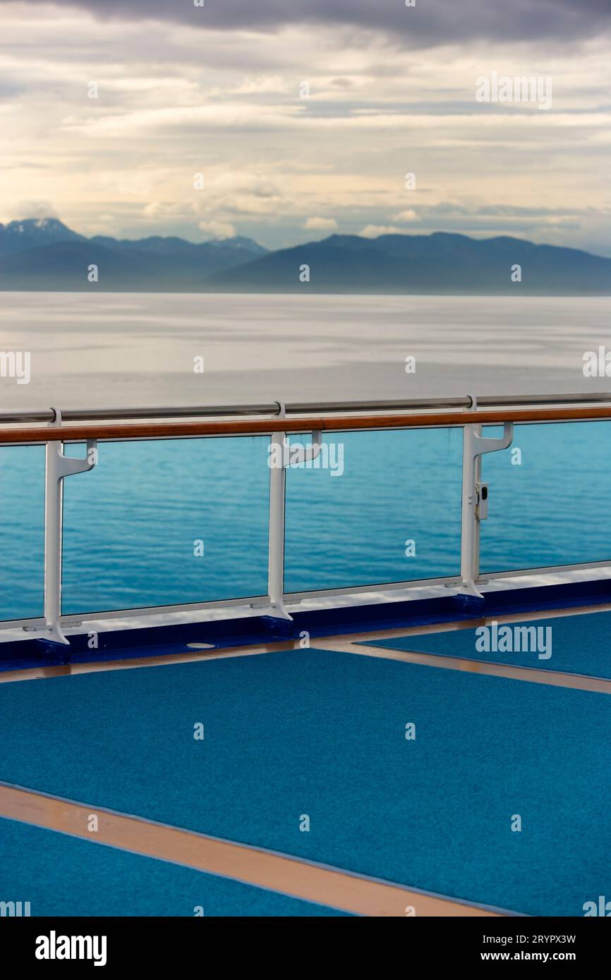 Cruise ship deck, hand railing, ocean and mountains along the inland ...