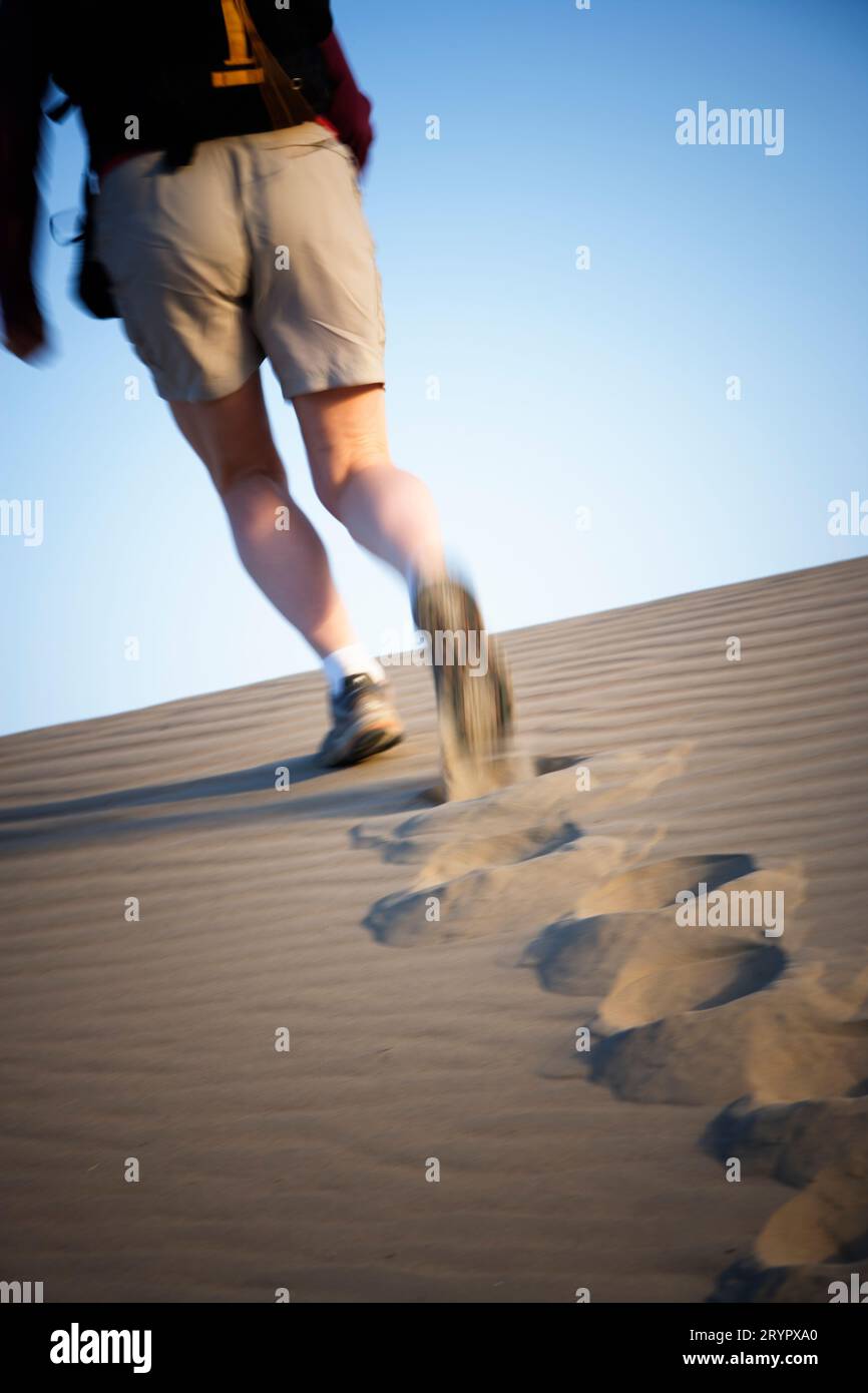 Rear view of a woman's legs walking up a sand dune in Death Valley ...