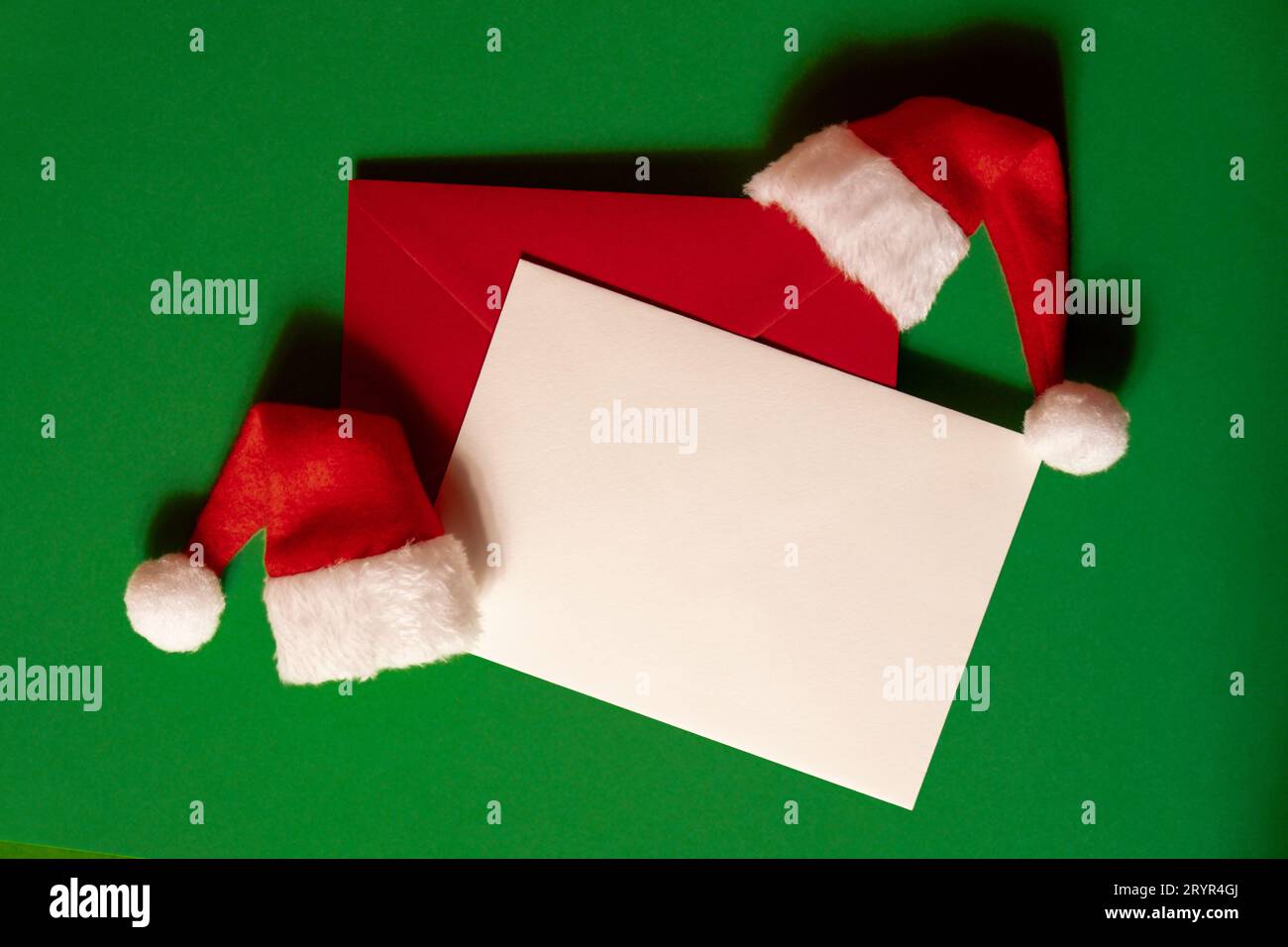 Santa hat with empty paper card note envelope on green background. Copy ...
