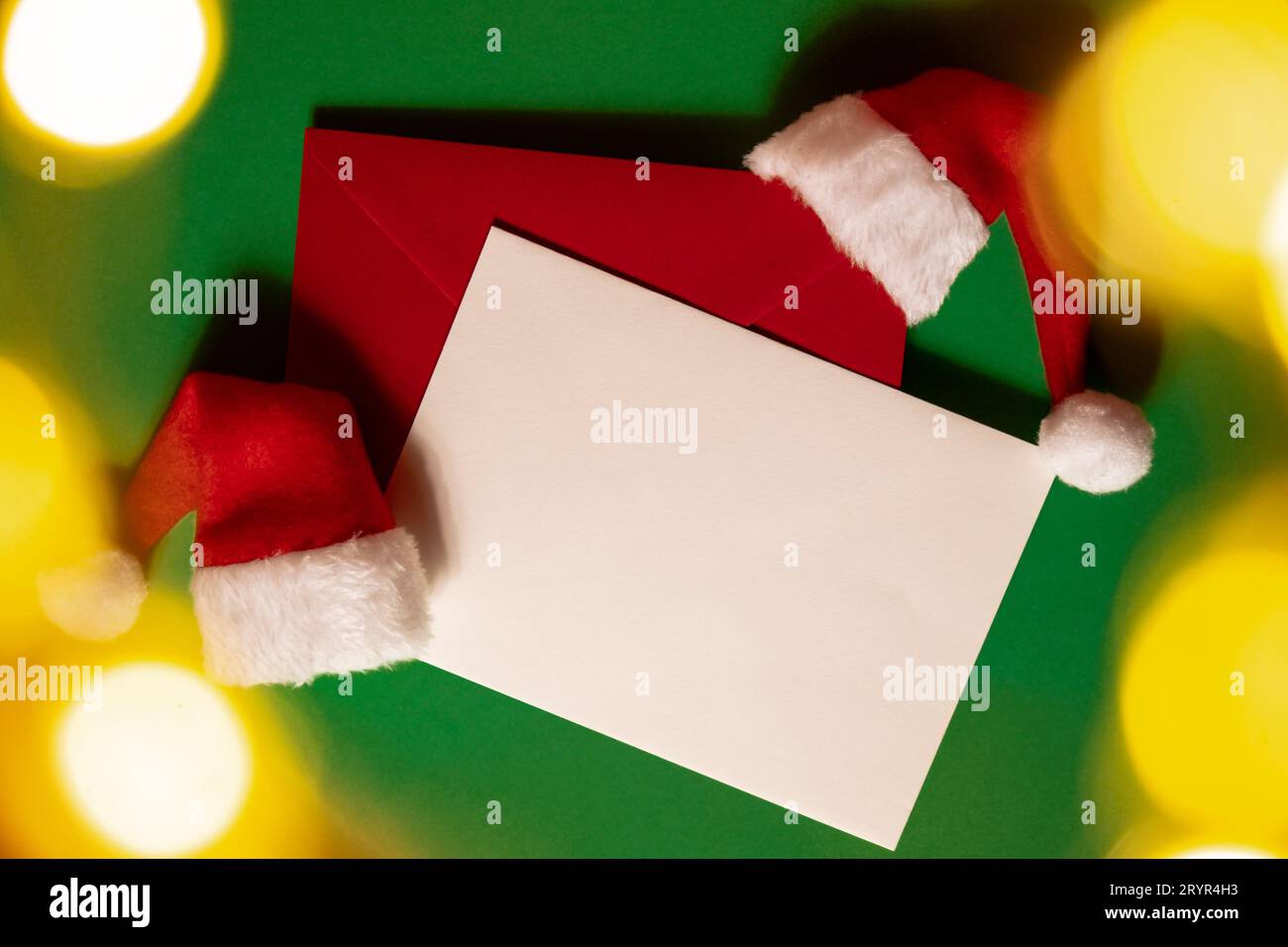 Santa hat with empty paper card note envelope on green background. Copy ...