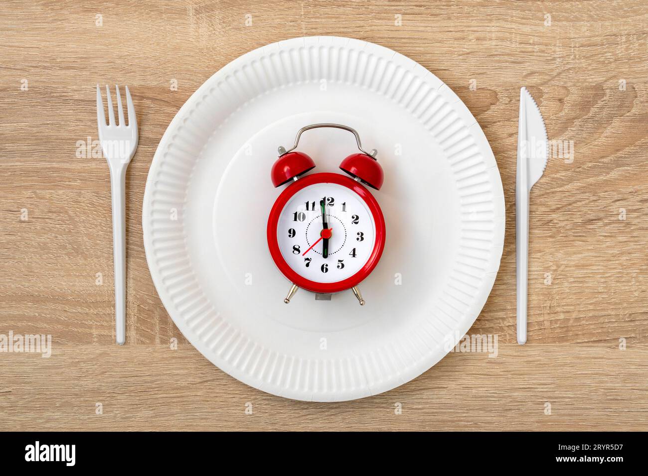 Concept of breakfast time with red alarm clock, disposable plate, fork ...