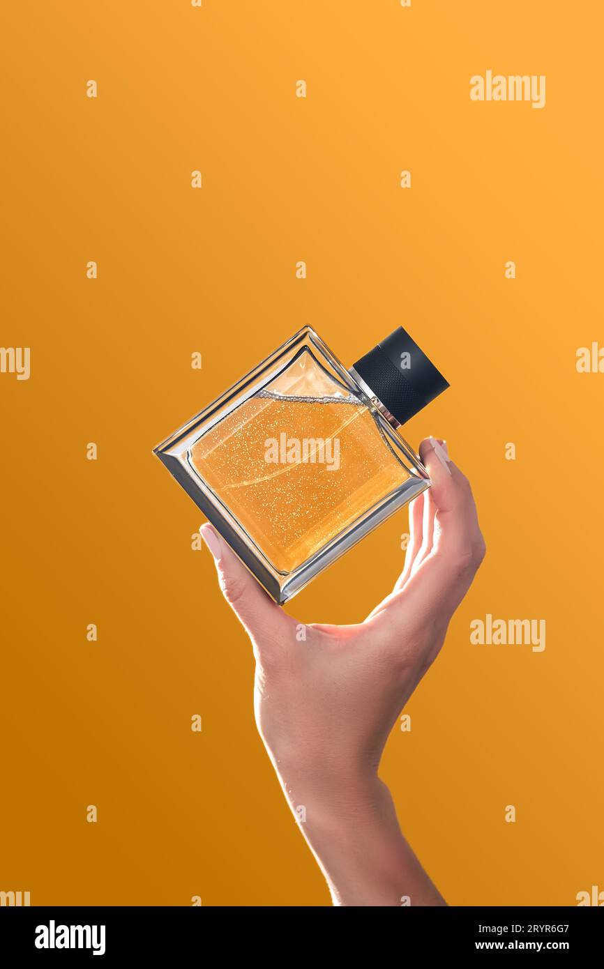 Perfume bottle in hands on an orange background Stock Photo - Alamy