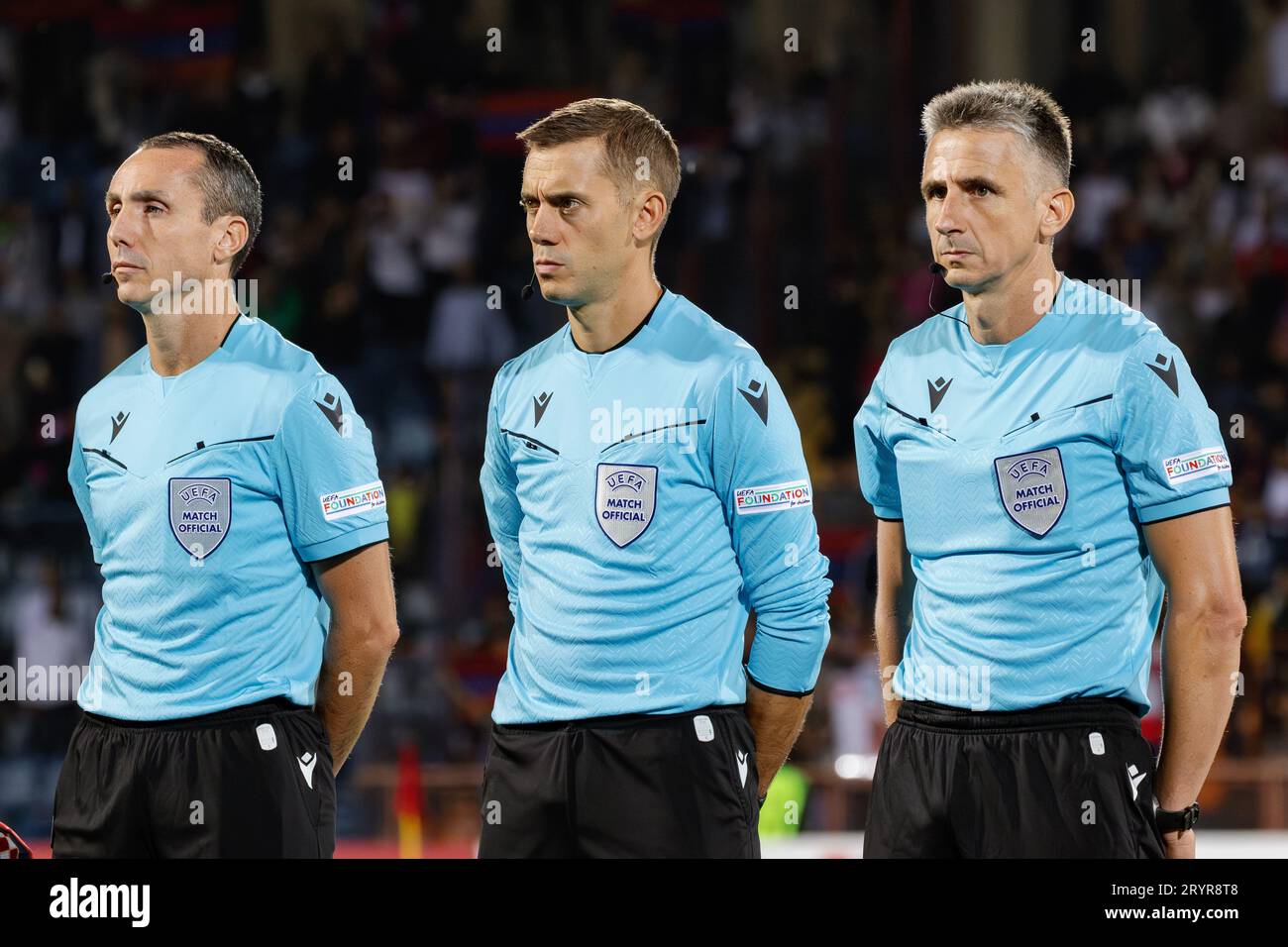 A team of referees standing on a grassy soccer field in blue uniforms ...
