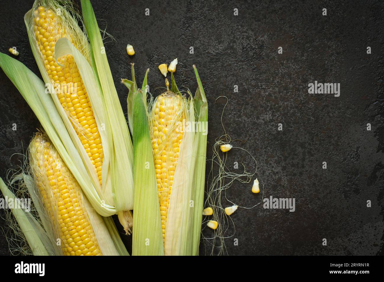 Ripe young sweet corn cob with leaves on black concrete background ...