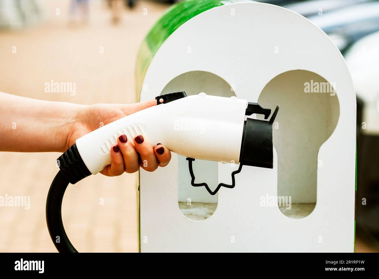 The female hand takes an electric vehicle charging cable. The driver ...