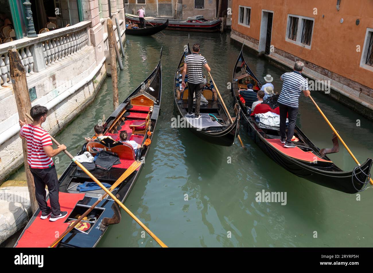 Three gondoliers steer their gondolas in a backwater canal in Venice in ...