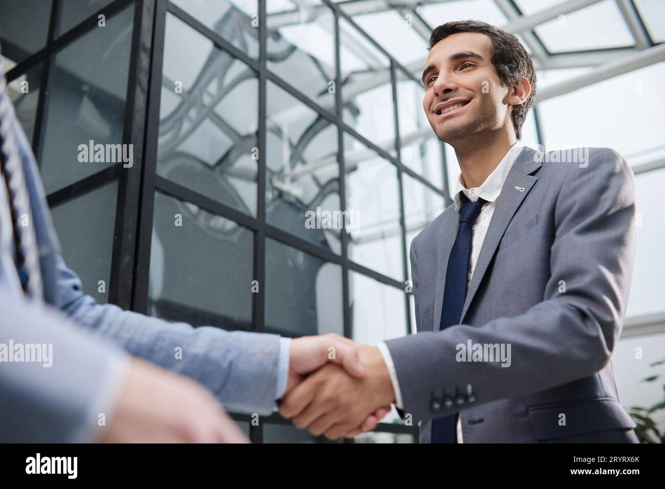 Businessmen shake hands, standing near a large office window Stock ...