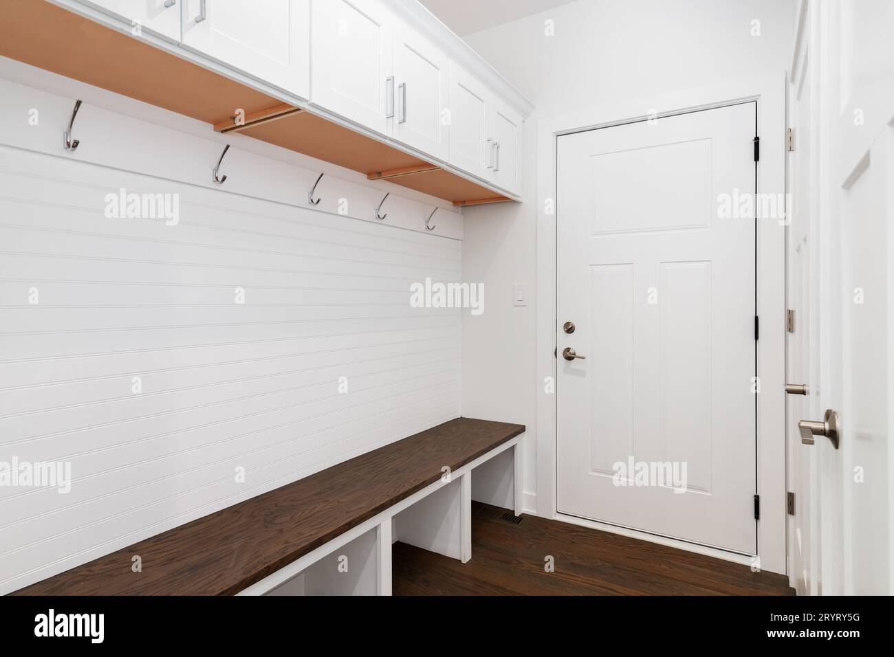 A mudroom with a dark wood floor and bench, white built-in cabinets and ...