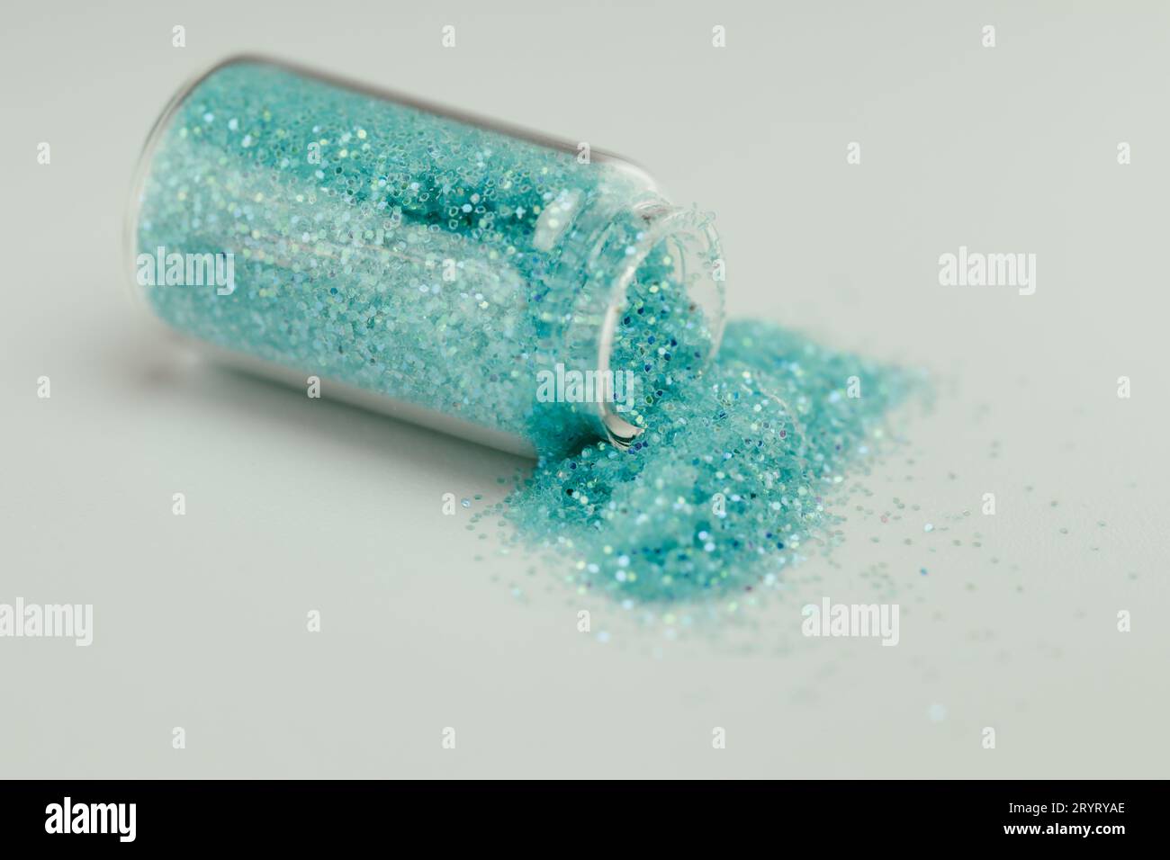 A jar of iridescent blue-green sparkles spilling out onto a white ...