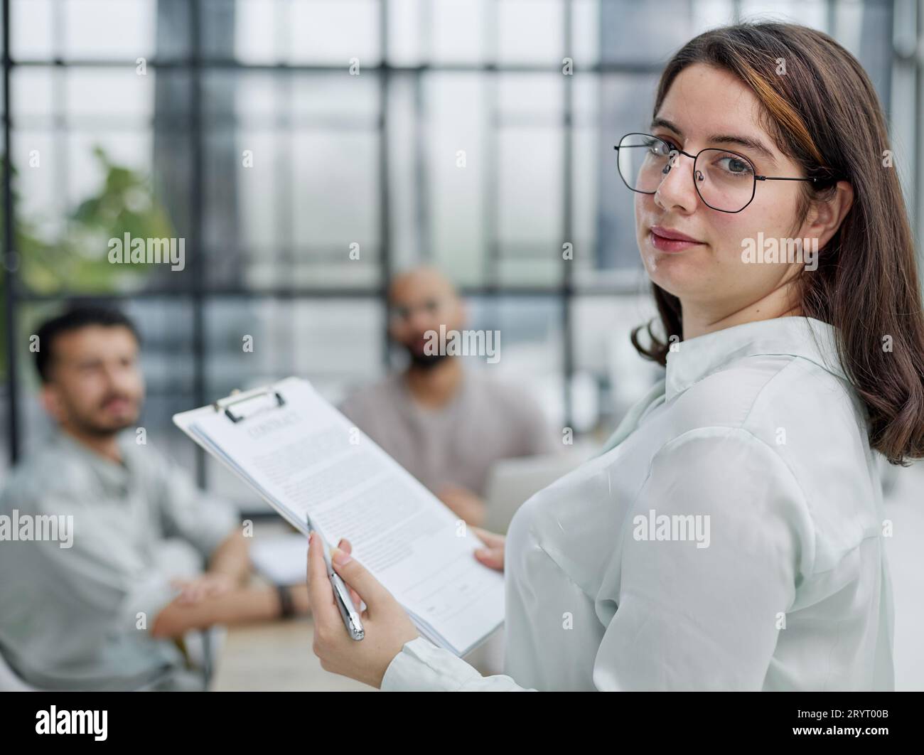 Positive manager girl is standing in a welllit office with a folder in ...