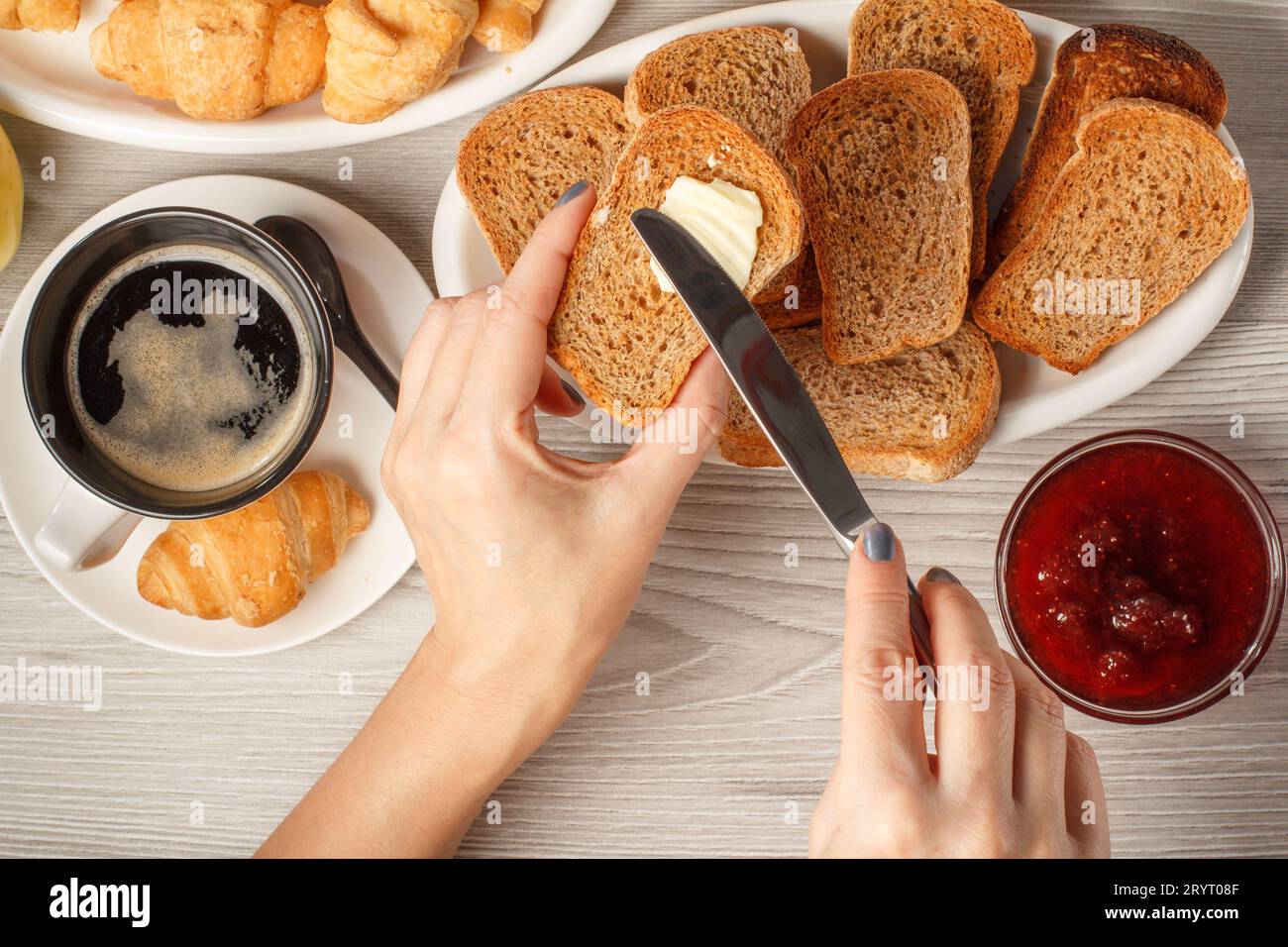 Female hands spreading butter on a toast with a cup of black coffee ...