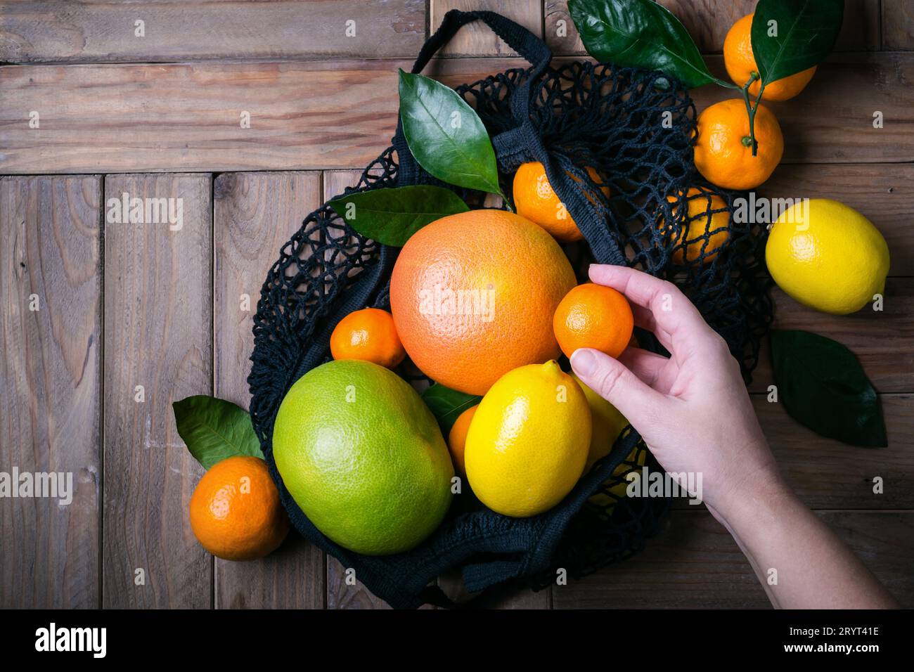 Female hand pulls citrus fruits out of textile mesh bag. Healthy food ...