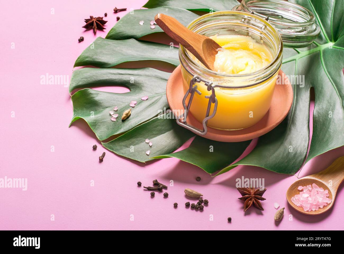 Ghee butter in a glass jar, pink salt and spices on pink background ...