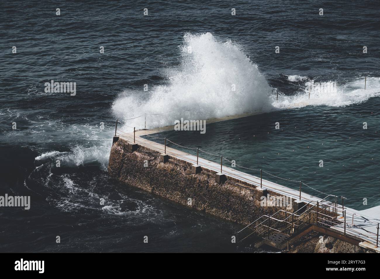 A large wave in the deep blue ocean crashing against a pool on ...