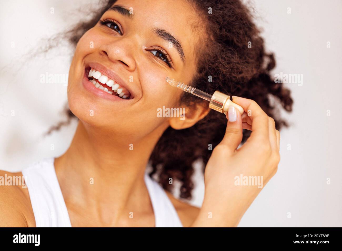 Cute smiling african young woman applies moisturizing serum from ...