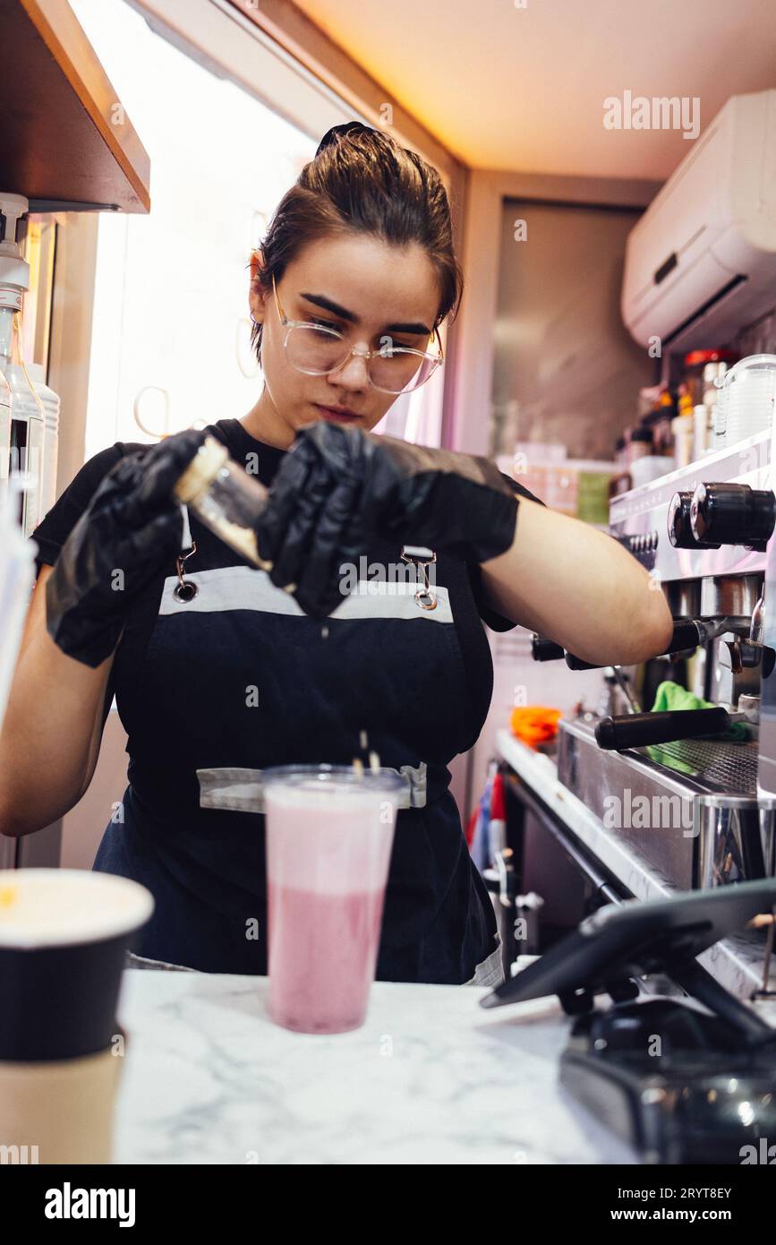 Brunette female barista decorates matcha cocktail with sweet topping ...