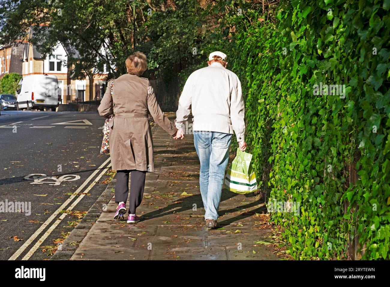 Rear view of elderly couple walking in London leafy street in autumn ...