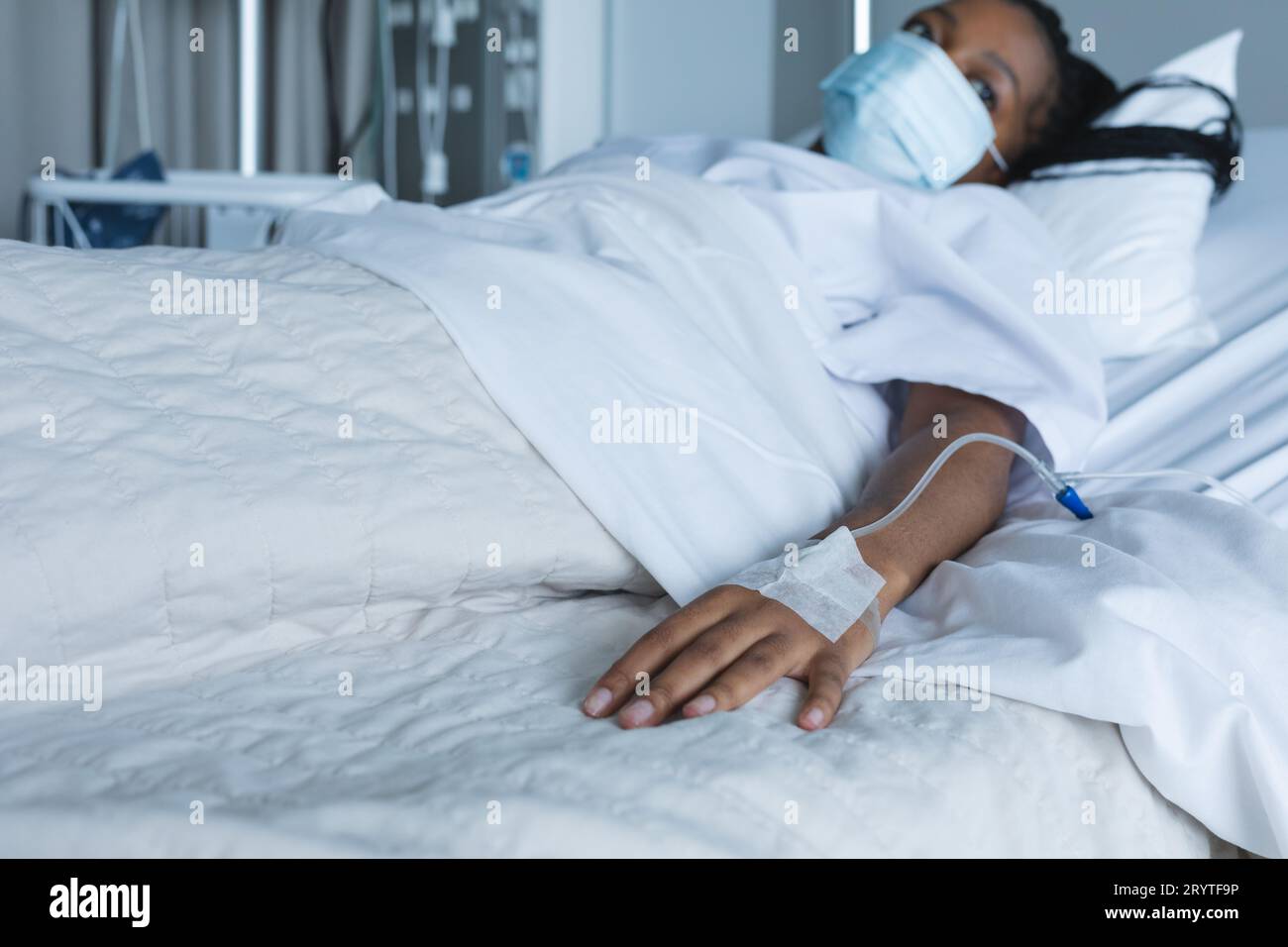 African american female patient wearing face mask, with drip on hand ...