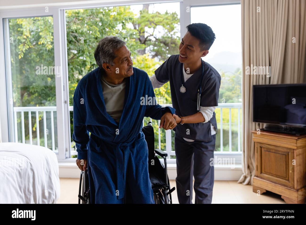 Diverse male doctor helping senior male patient getting up from ...
