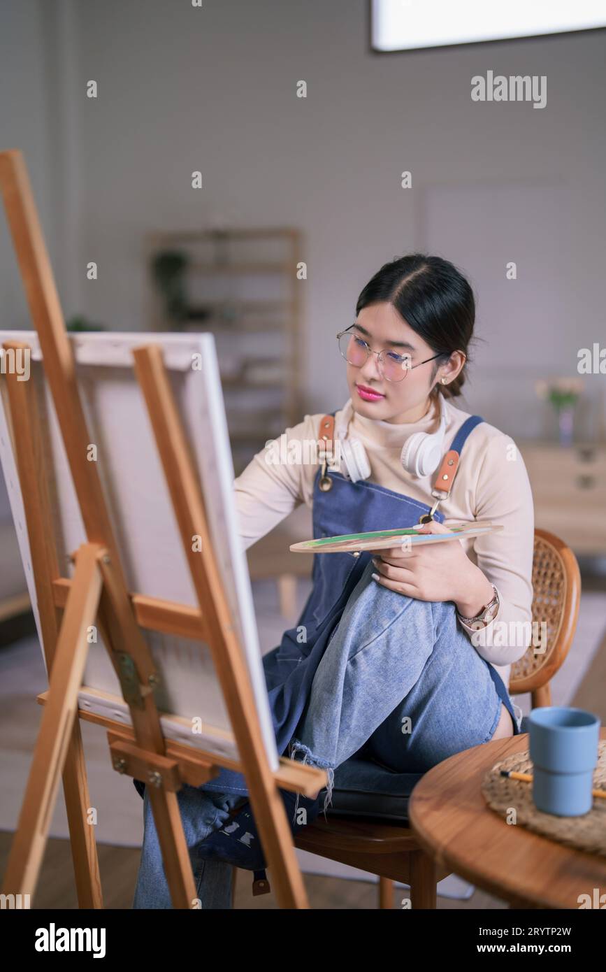 Young asian female artist wear headphone in her neck and use paintbrush ...