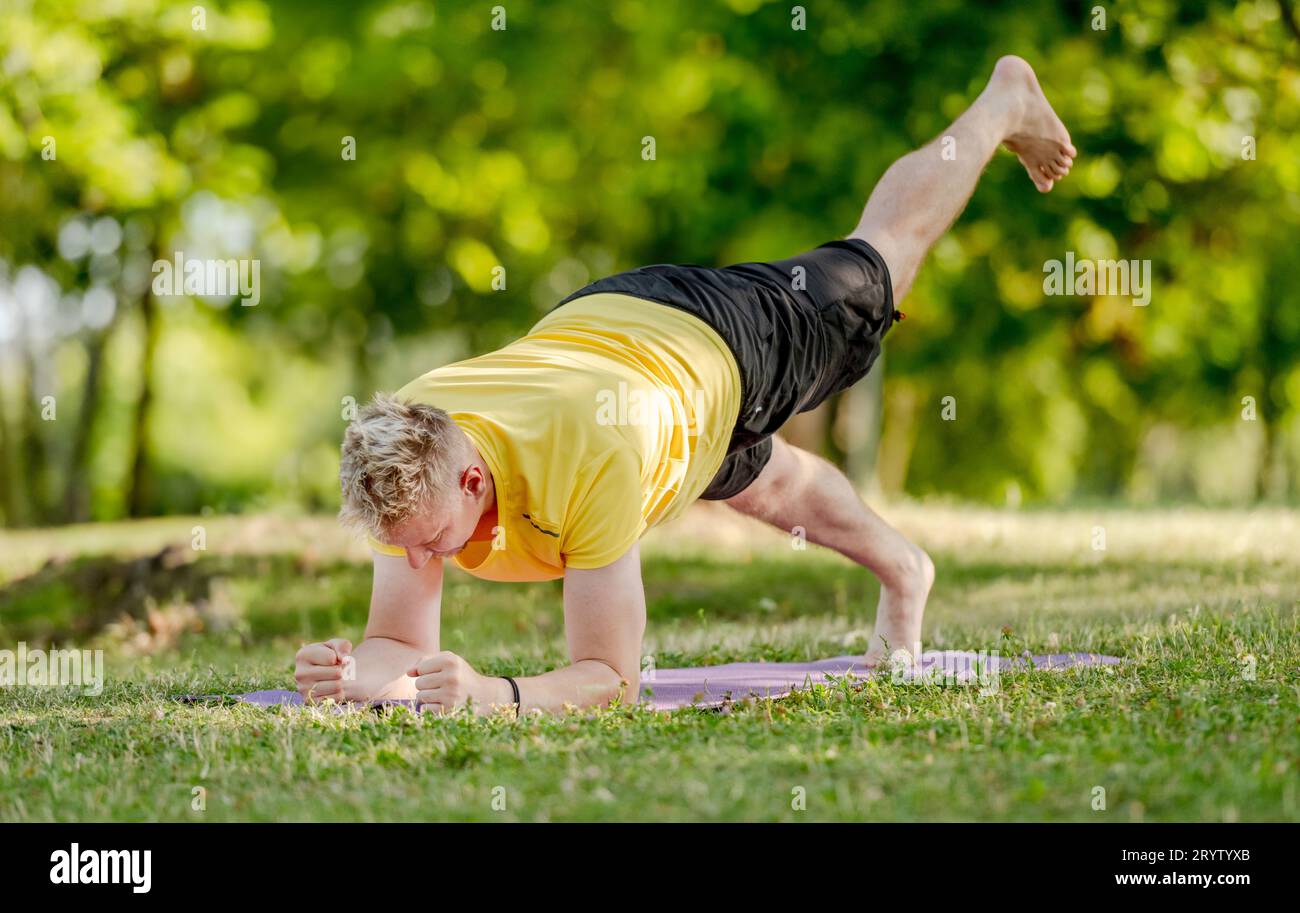 Man standing in plank position and practicing yoga outdoors at summer ...