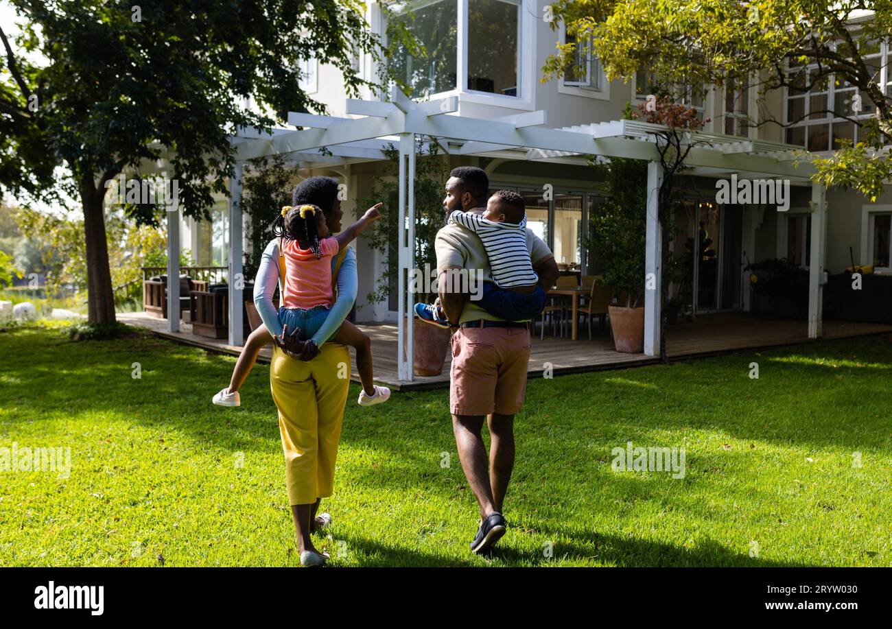 Rear view of african american mother and daughter piggybacking children ...