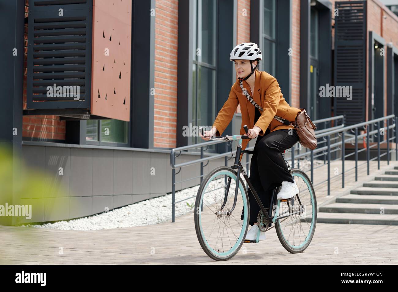 Young woman in formalwear and safety helmet sitting on bicycle and ...