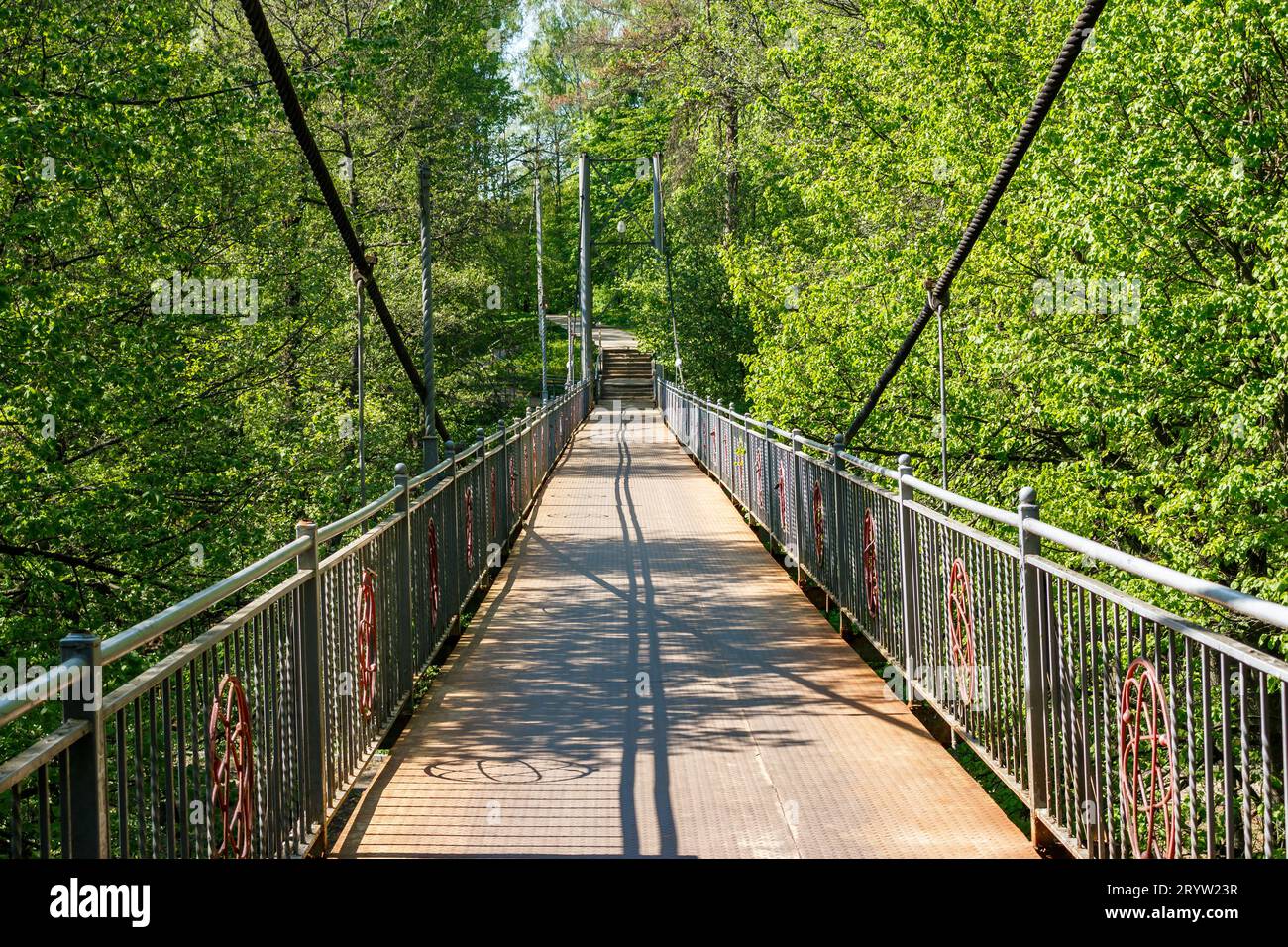 A metal pedestrian bridge over a ravine surrounded by green trees ...