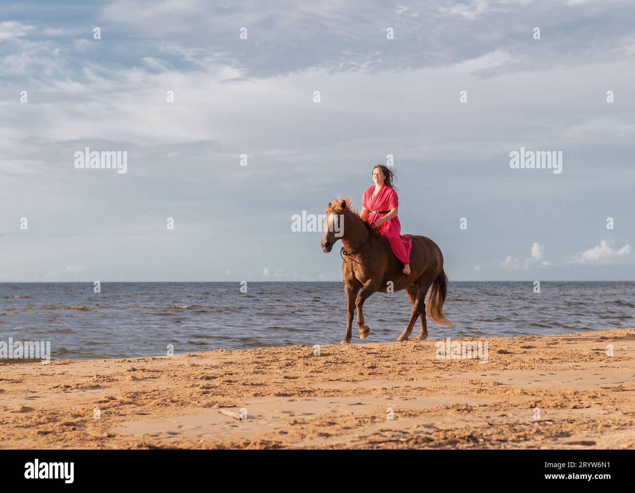 An adult leisurely riding a horse along a sandy beach shoreline, with ...