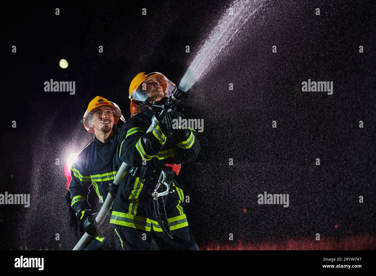 Firefighters using a water hose to eliminate a fire hazard. Team of ...