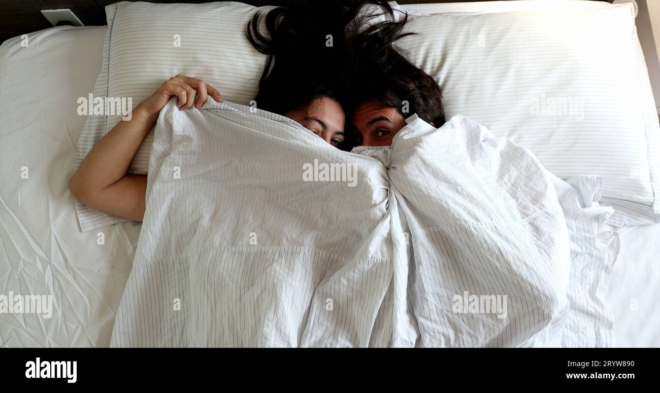 Fun loving young married couple hiding under blanket in bed, top view ...