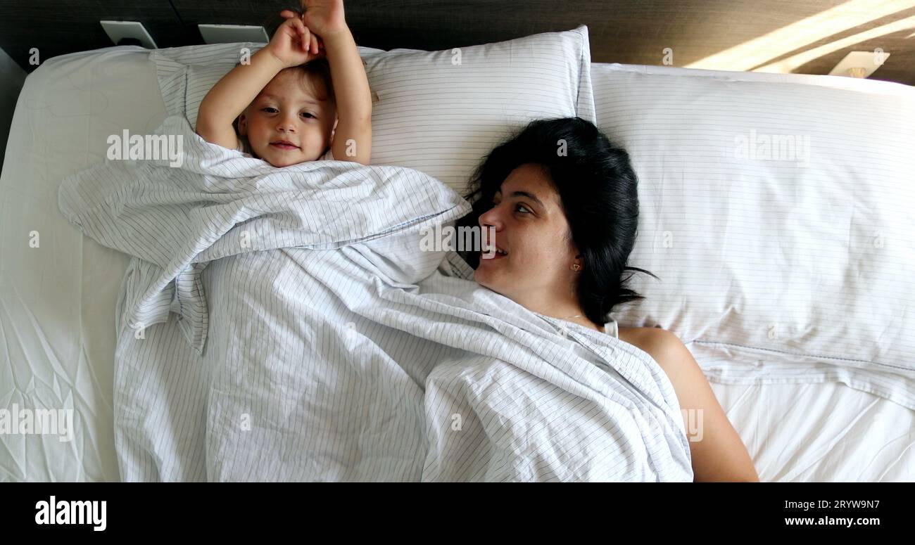 Cute baby and mother in bed blinking to camera. Top view Stock Photo ...