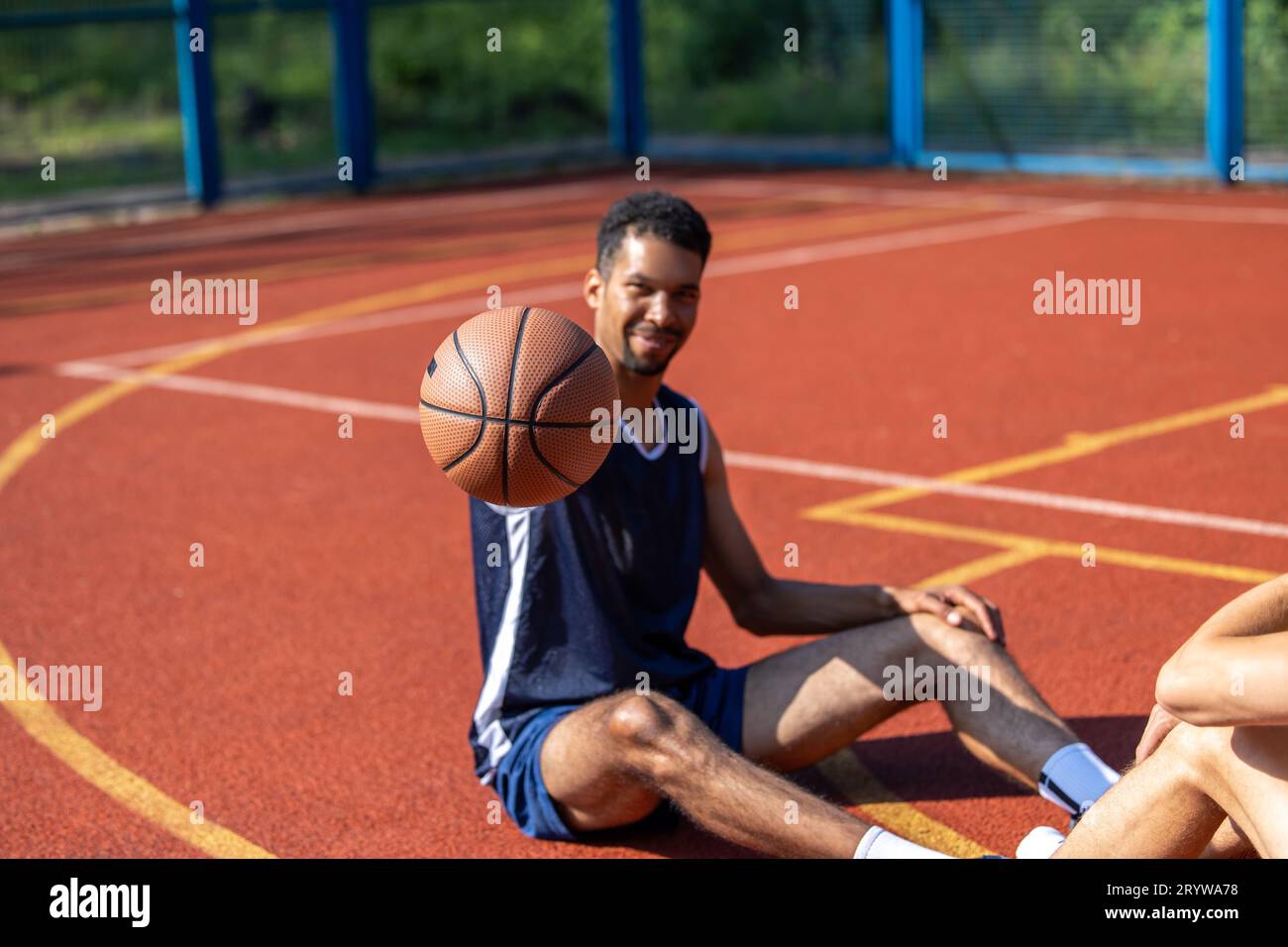 Cheerful man resting sitting on the basketball court after playing game ...