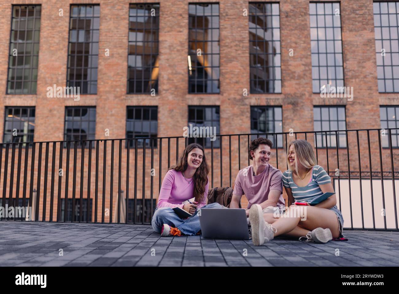 Young stylish generation Z students sitting in front of school building ...