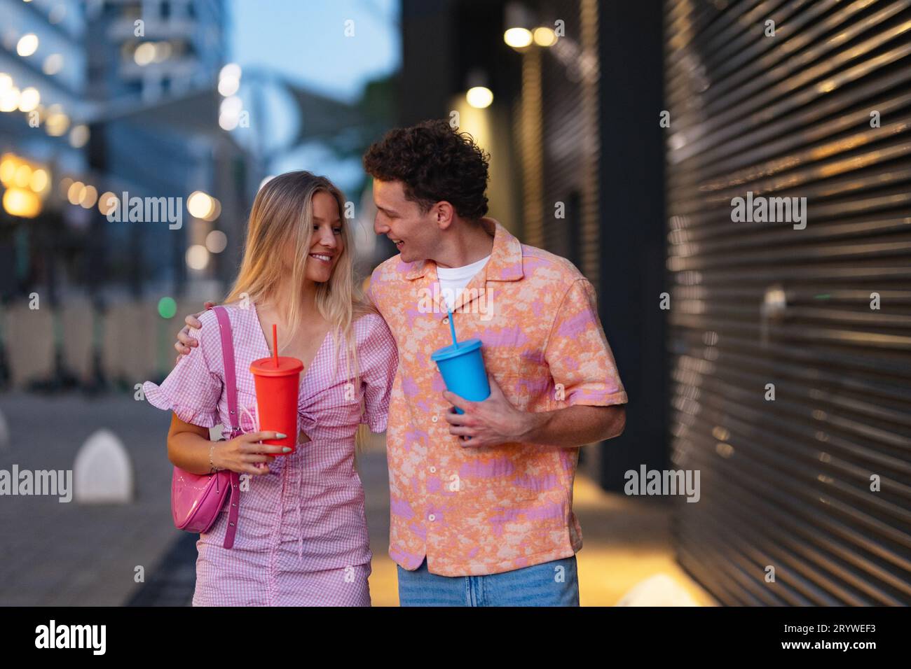 Gen Z couple in pink outfits leaving the cinema with drinks in hand ...