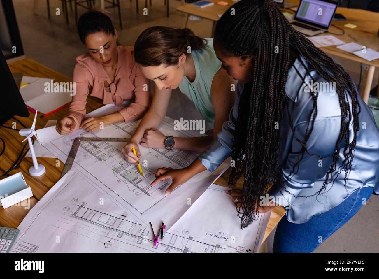 Diverse female architects in discussion using blueprints in casual ...